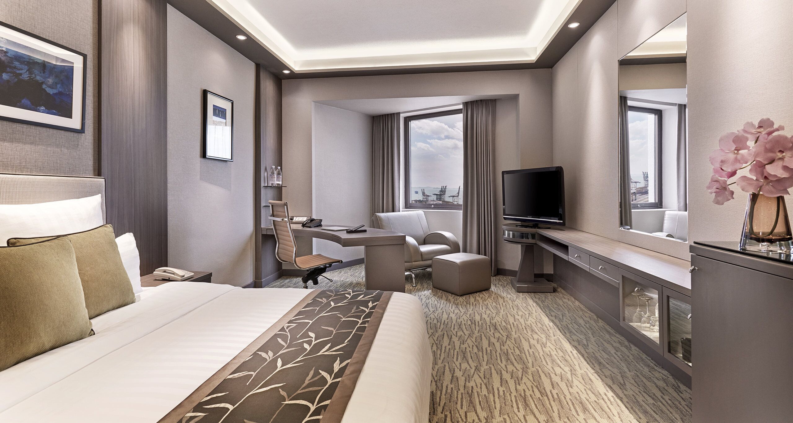 Quarto de hotel com uma cama grande, uma escrivaninha com cadeira, televisão e vista para a cidade.