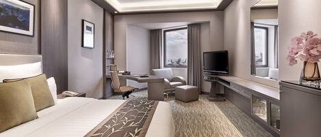 Quarto de hotel com uma cama grande, uma escrivaninha com cadeira, televisão e vista para a cidade.
