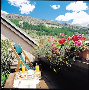 Terraço com mesa posta para café da manhã, com vista para uma paisagem montanhosa.