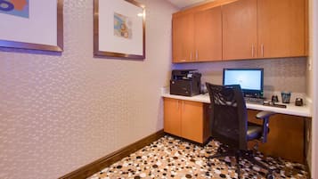 Um escritório pequeno com mesa, cadeira, computador e impressora.