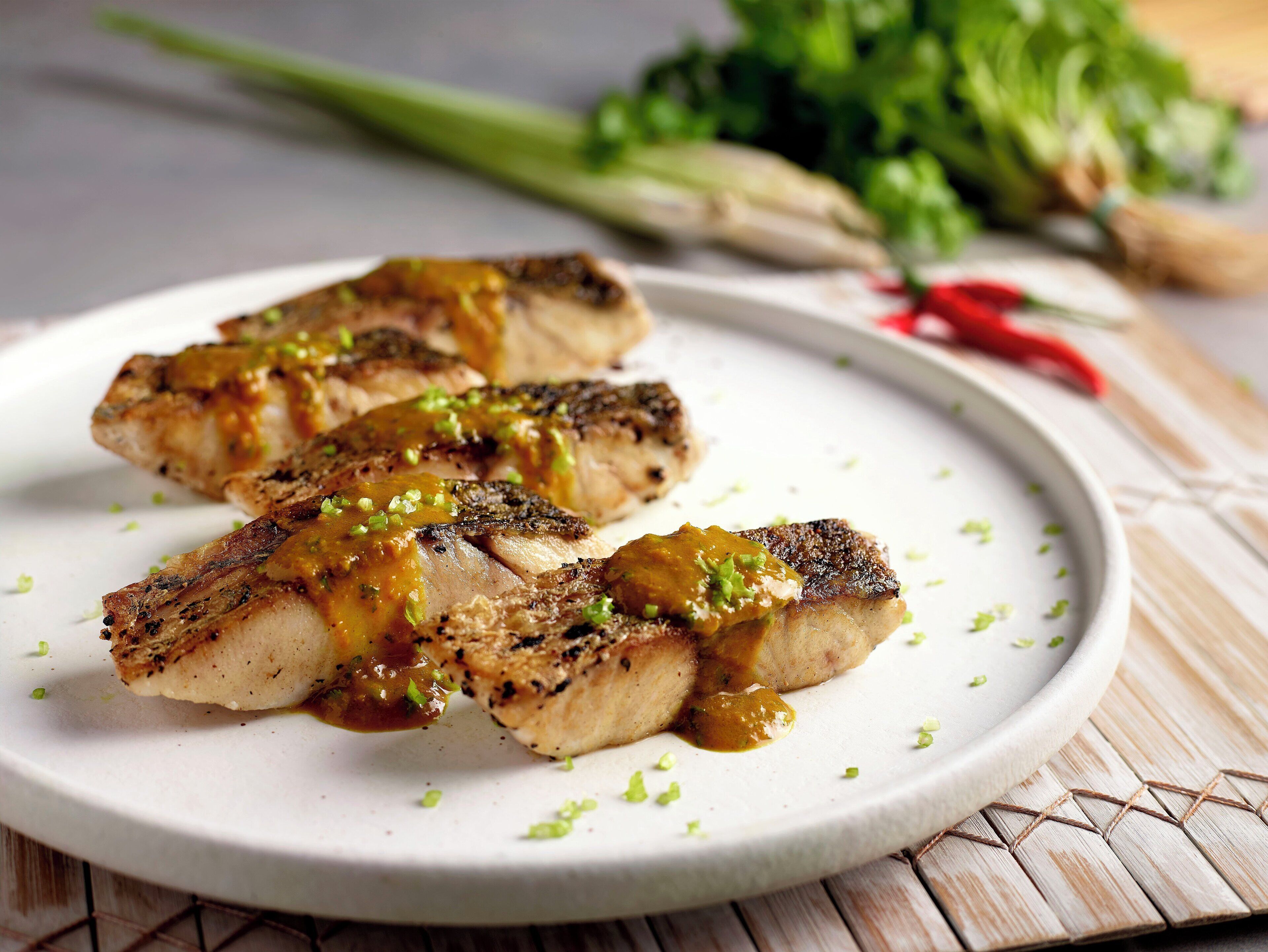 Prato de peitos de frango grelhados com molho, guarnecido com ervas verdes, sobre um prato branco.
