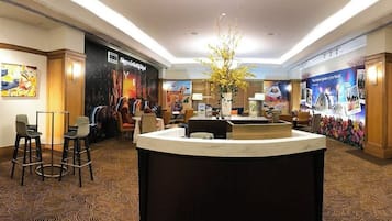 Um hall de hotel com balcão de recepção, área de bar e sofás.