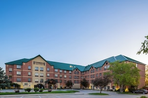 Um hotel Staybridge Suites com fachada de tijolos, telhado verde e estacionamento.