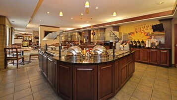 Área de buffet com ilha central, diversas opções de assentos e uma televisão presa na parede.