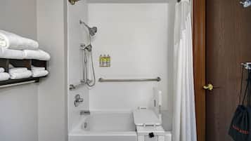Área de banho com banheira, porta-toalhas com toalhas dobradas, painel de comando do chuveiro e porta com uma toalha pendurada.