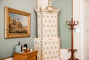 Quarto com quadro emoldurado, um pilar branco decorativo, mesa de madeira com torradeira e um suporte alto com gancho.