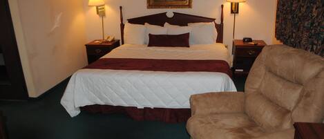Quarto de hotel com uma cama grande, duas mesas de cabeceira com luminárias, uma cadeira e um quadro na parede.