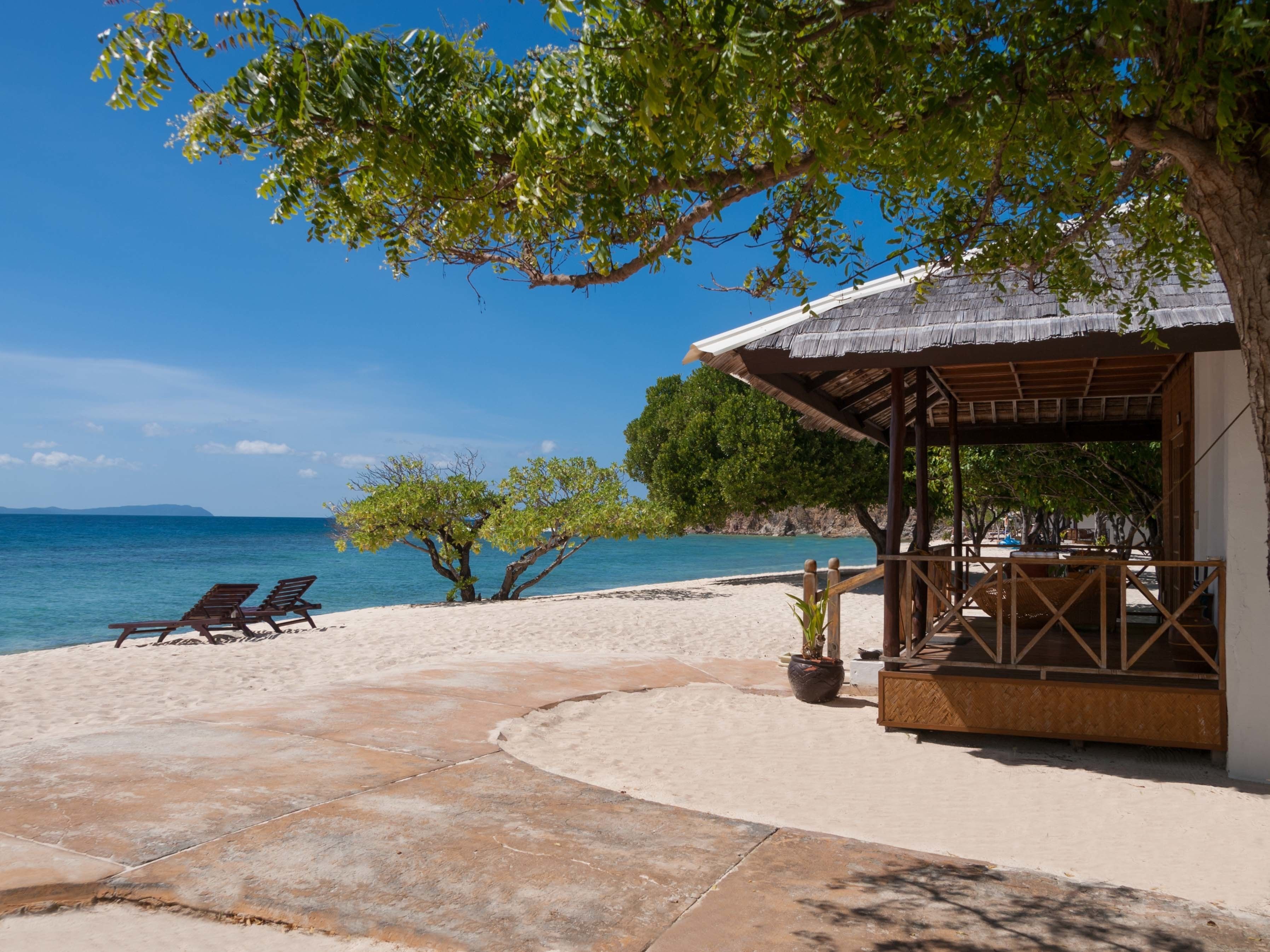 Um resort à beira-mar com uma área de estar coberta, uma estrutura com telhado de palha e vista clara para o oceano.