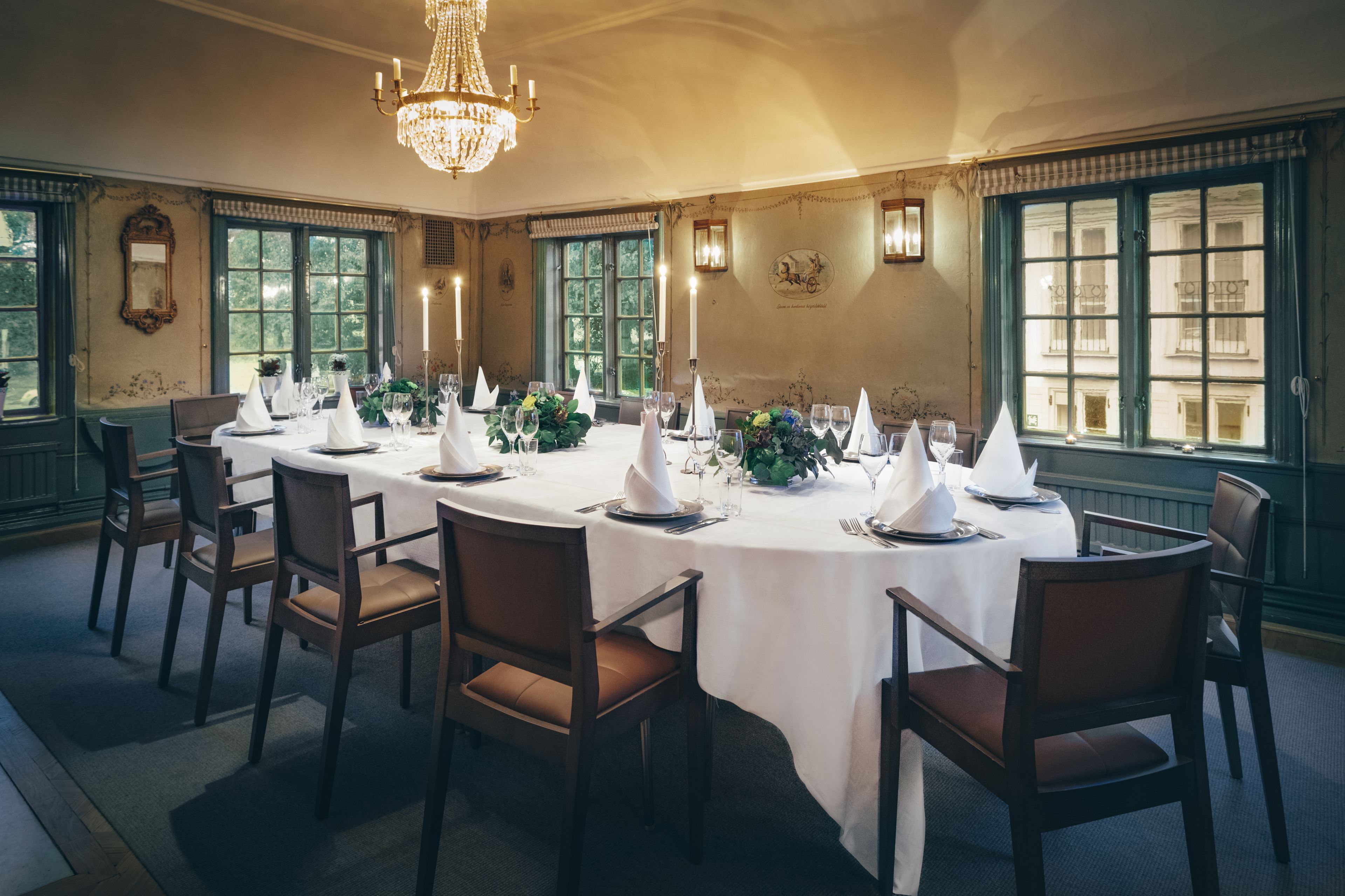 Uma sala de jantar formal com uma mesa redonda posta para seis pessoas, rodeada por cadeiras de madeira com assentos acolchoados.