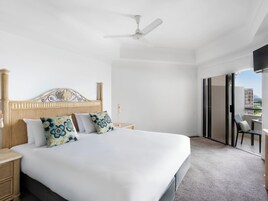 Quarto de hotel com uma cama grande, um ventilador de teto, uma mesa de cabeceira e vista para o exterior através de uma porta de correr.
