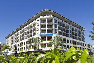 Um hotel com vários andares, varandas, uma placa com a inscrição 'Mantra Esplanade' e vegetação exuberante na frente.