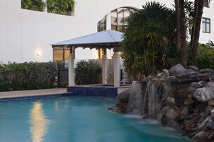 Piscina com cascata, cercada por pedras e plantas.