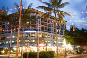 Um hotel com vários andares, varandas, palmeiras e luzes de Natal.
