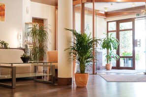 Um lobby moderno com um sofá, mesa de centro de vidro e plantas em vasos.