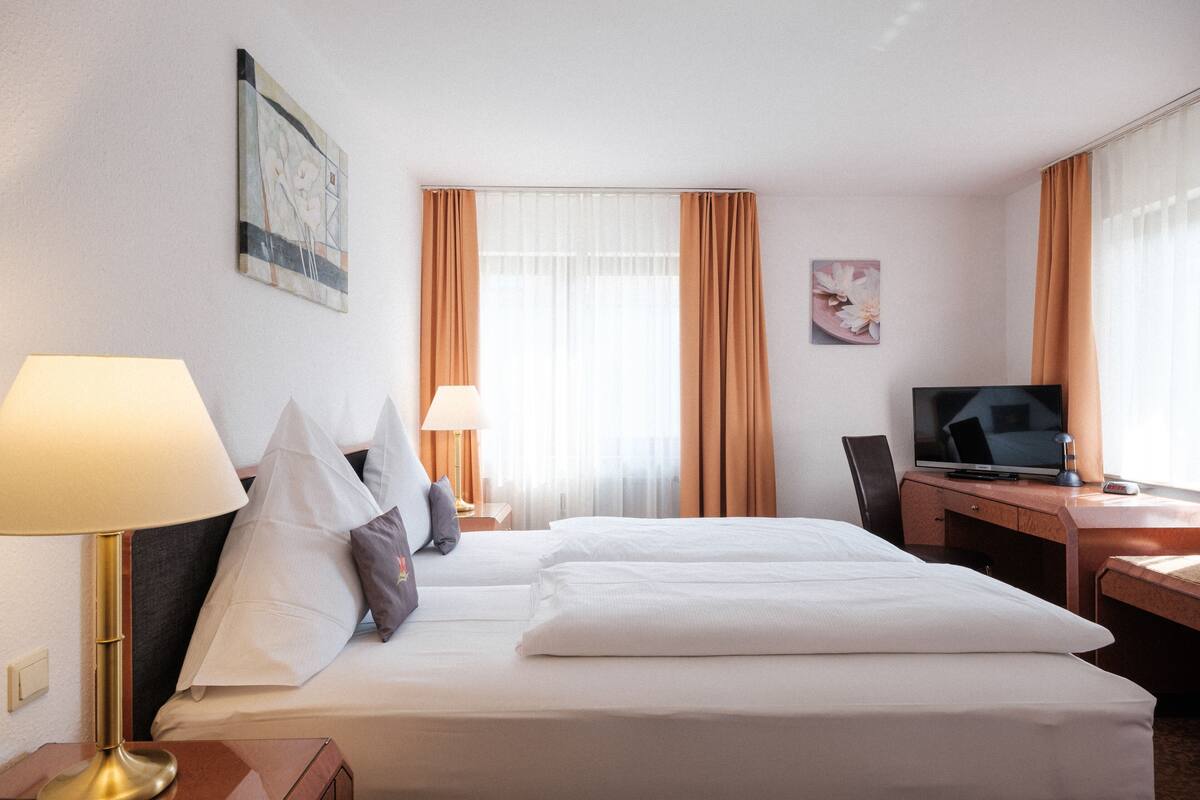 Quarto de hotel com duas camas, uma mesa de escritório, um computador, uma televisão e um abajur.