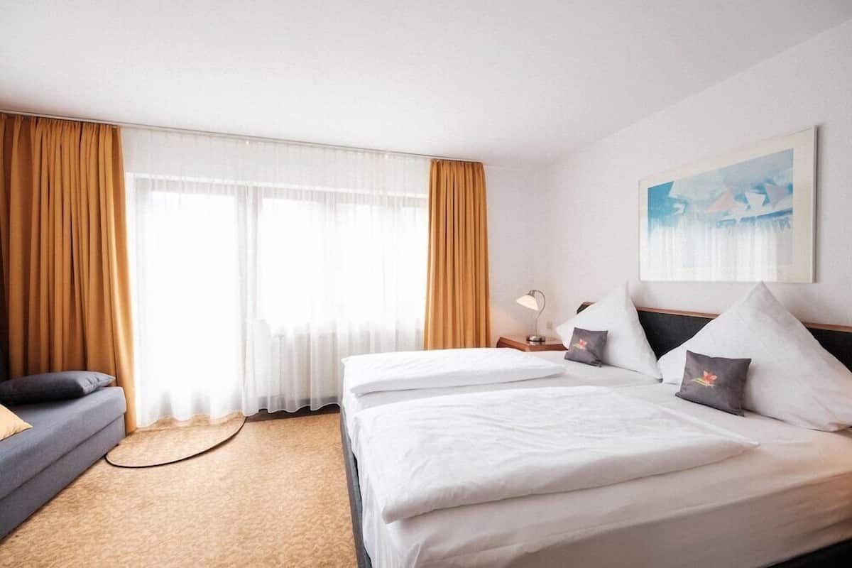 Quarto de hotel com cama, sofá, luminária e um quadro na parede.