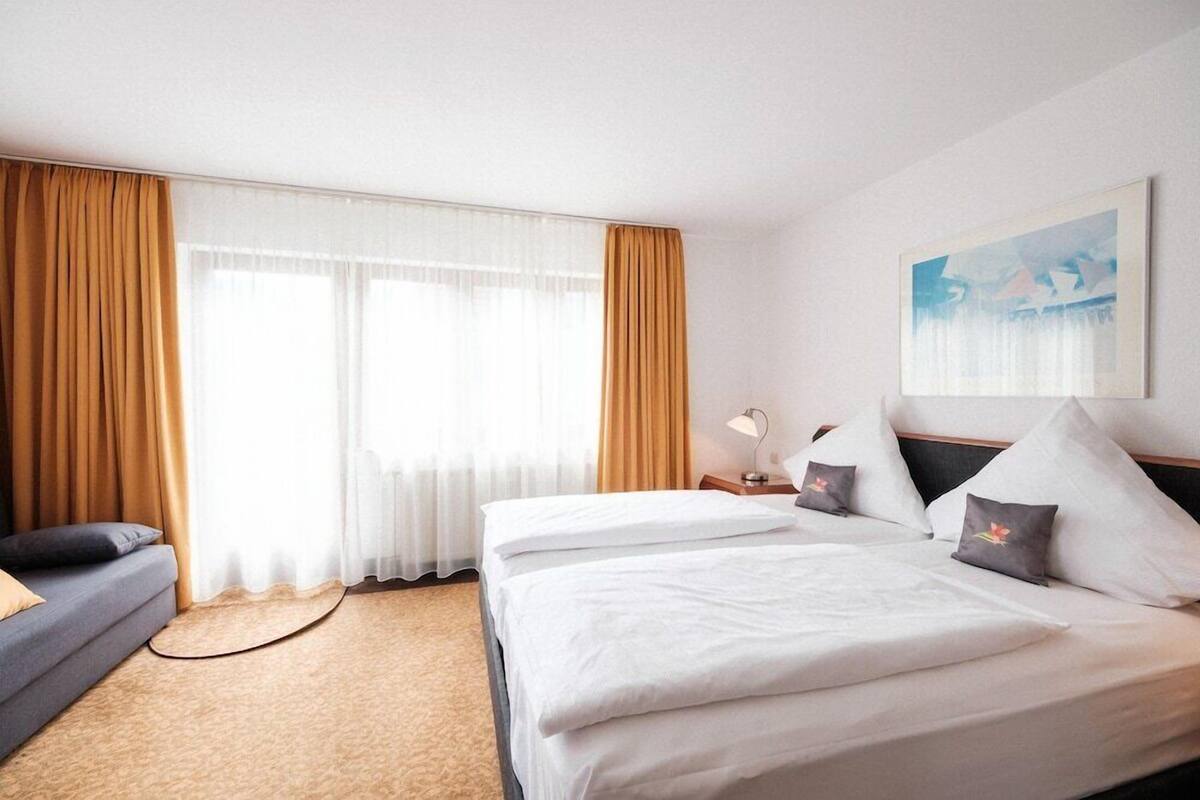 Quarto de hotel com cama, sofá, luminária e um quadro na parede.