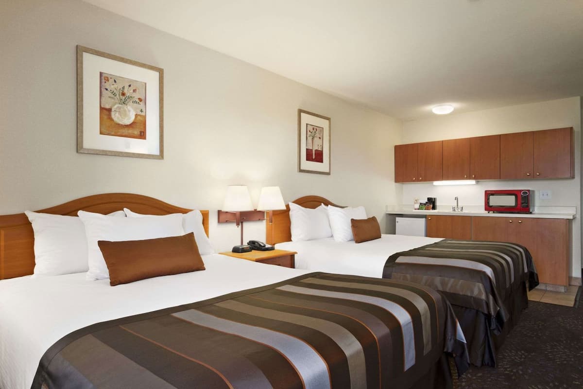 Quarto de hotel com duas camas, uma kitchenette e obras de arte nas paredes.