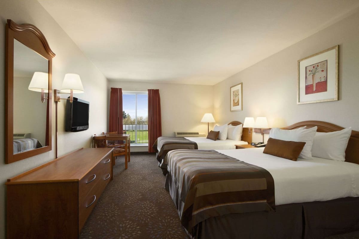 Quarto de hotel com duas camas, uma escrivaninha, uma TV e uma janela com cortinas.