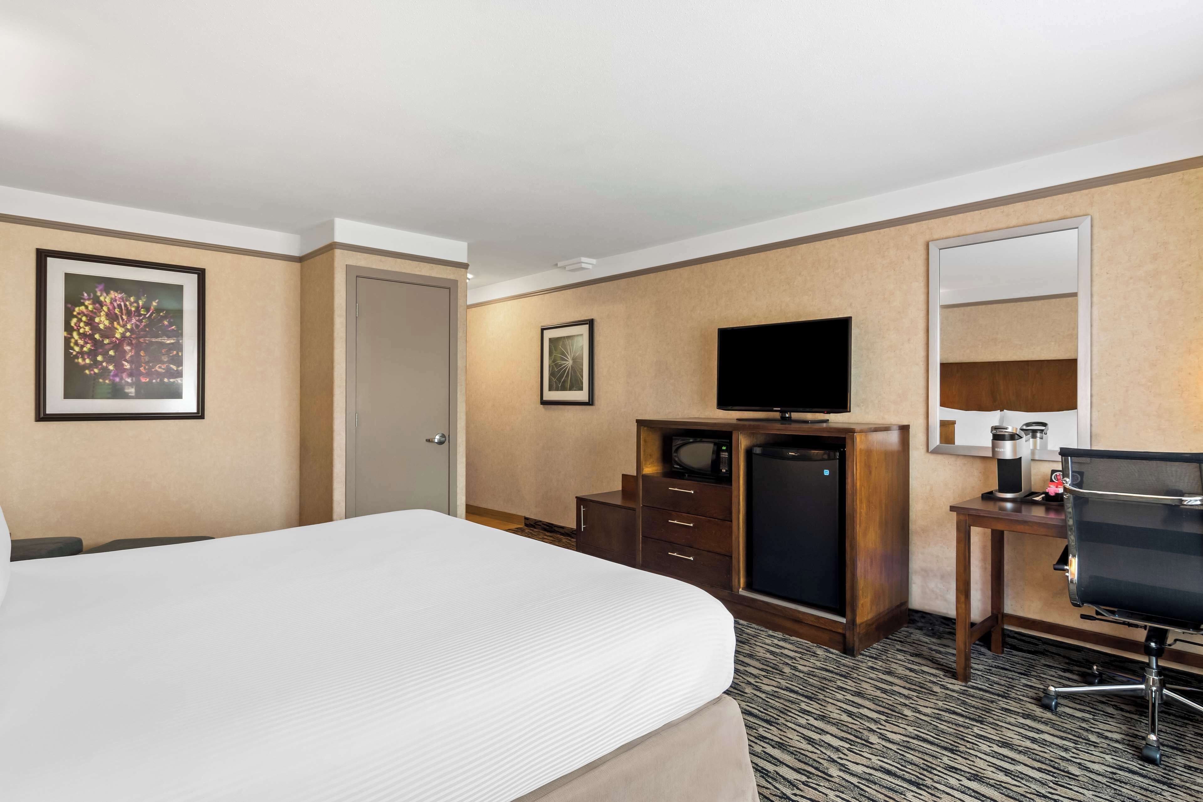 Quarto de hotel com cama, escrivaninha, computador, televisão e espelho.