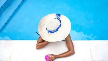 Uma pessoa sentada à beira da piscina, usando um chapéu de palha e segurando uma bebida.