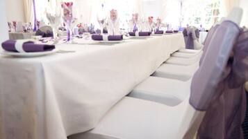Uma longa mesa com toalhas brancas e guardanapos roxos, preparada para um evento formal.