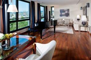 Uma sala de estar ampla com um piano de cauda, uma mesa de centro de vidro e vista para o horizonte urbano por grandes janelas.