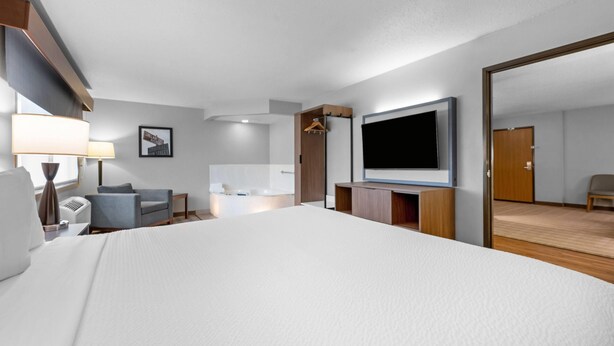 Quarto de hotel com uma cama grande, televisão de tela plana, escrivaninha com cadeira, sofá, abajur e espelho.