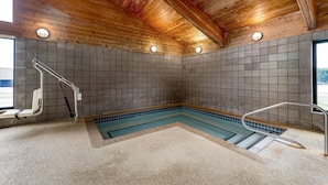 Uma área de spa com teto de madeira, paredes azulejadas, piscina e um banco acessível para cadeiras de rodas.