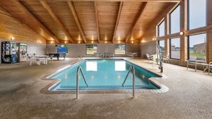 Uma piscina interior com teto de madeira, paredes revestidas de azulejos e vista para o exterior.