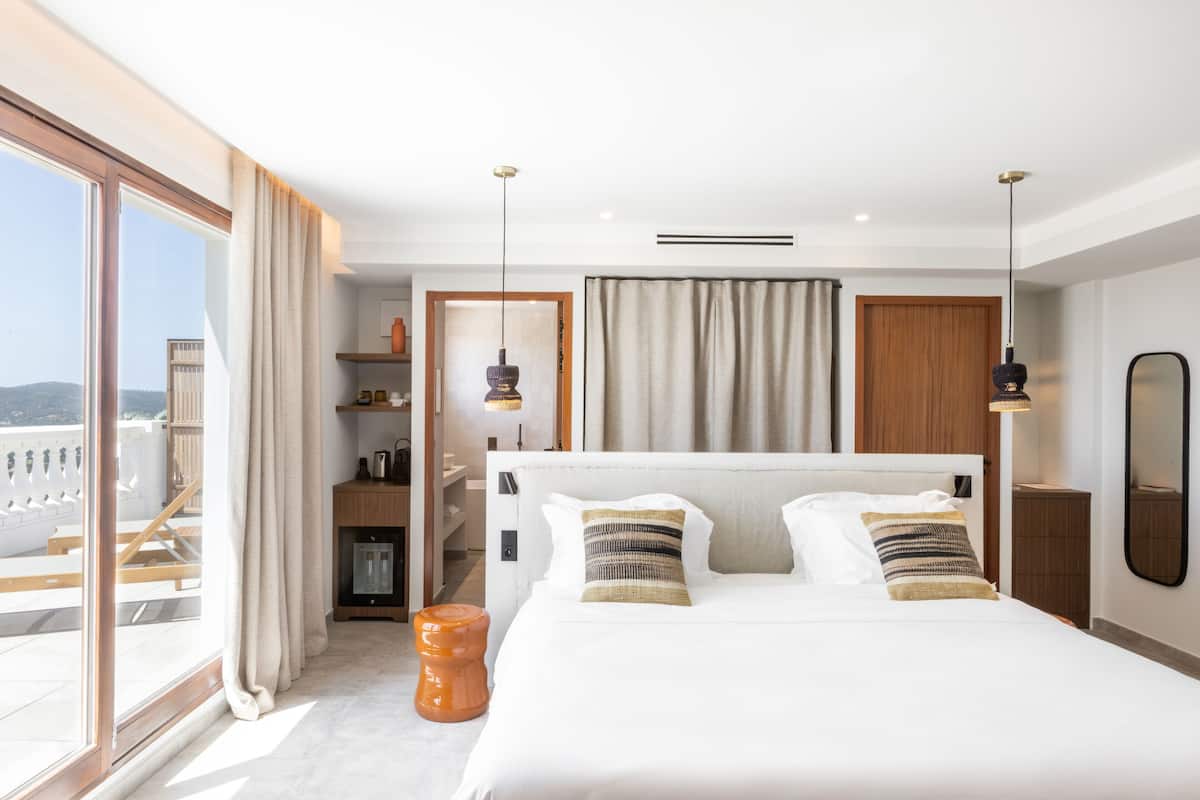 Quarto de hotel moderno com uma cama grande, um guarda-roupa, uma penteadeira e uma janela ampla com vista para a cidade.