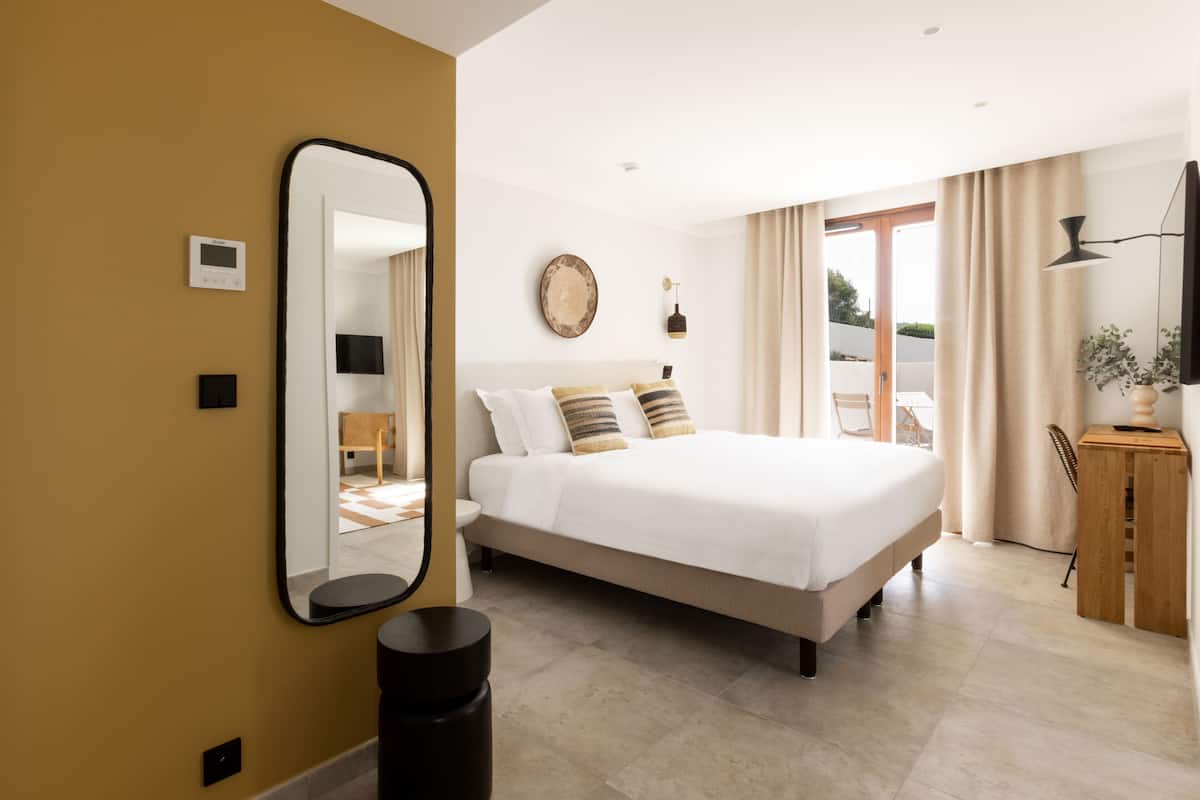 Quarto de hotel moderno com uma cama grande, um espelho, uma escrivaninha pequena e vista para o exterior.