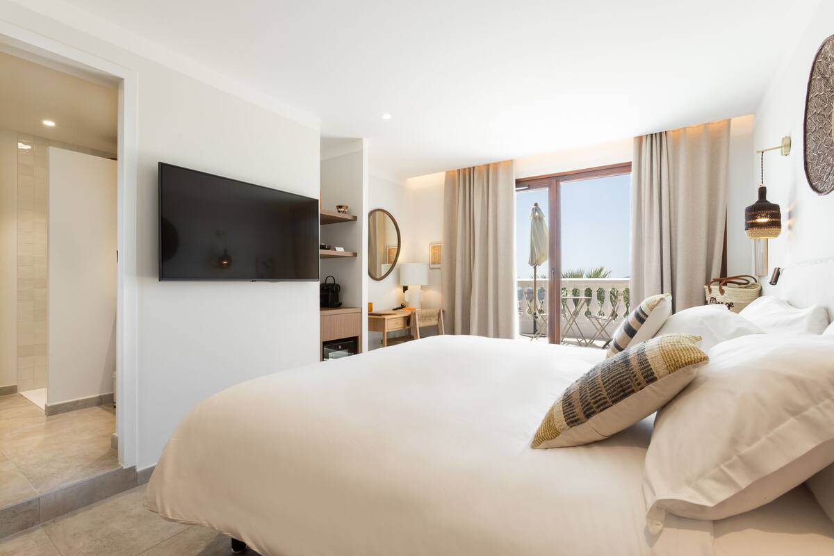 Quarto de hotel moderno com uma cama grande, televisão de tela plana, escrivaninha com cadeira e varanda com vista.