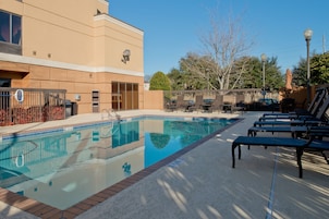 Piscina com espreguiçadeiras, cerca e edifício com fachada bege.