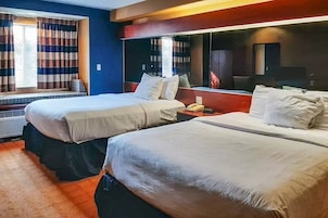 Quarto de hotel com duas camas, um espelho grande, mesa de cabeceira com telefone e janela com cortinas listradas.