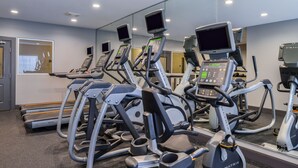 Uma academia com várias esteiras e aparelhos elípticos, equipada com telas digitais e painéis de controle.