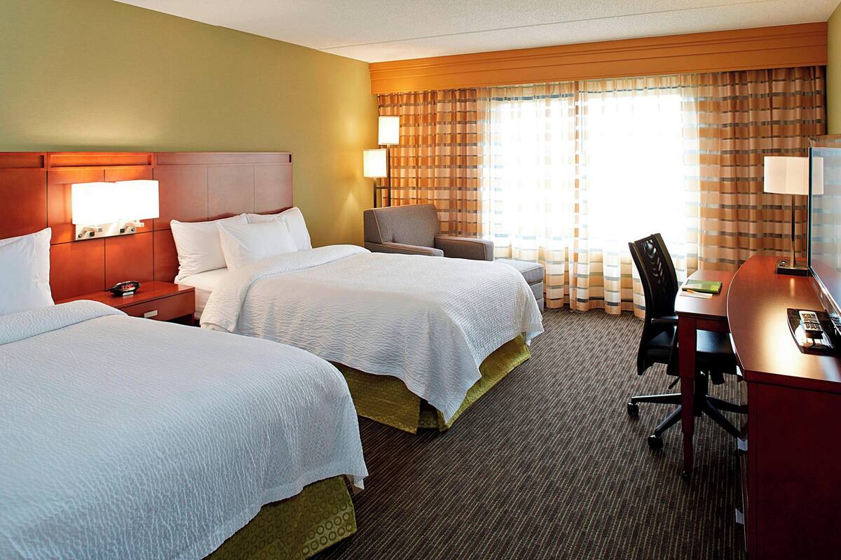 Quarto de hotel com duas camas, uma escrivaninha e uma cadeira.