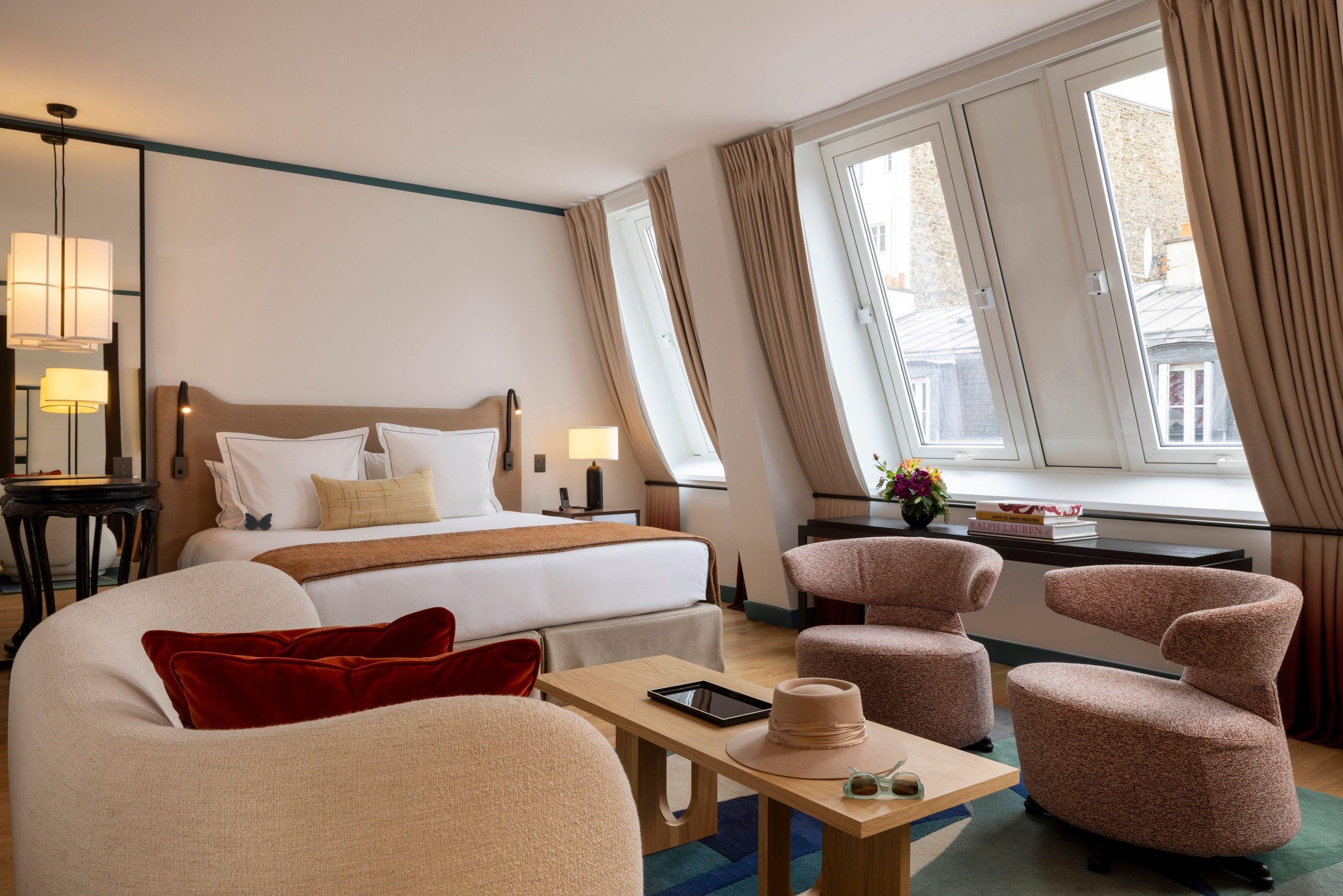 Quarto de hotel com cama, escrivaninha, cadeira e janela com cortinas.