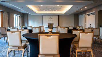 Uma sala de conferências com uma grande mesa oval rodeada por cadeiras, um logotipo emoldurado na parede e um chão coberto de carpete.