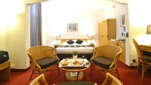 Quarto de hotel com cama, duas cadeiras, uma mesinha com um tabuleiro de comida, escrivaninha e guarda-roupa.