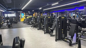 Uma academia com diversos aparelhos de ginástica, um relógio digital e uma placa com a inscrição 'Fitness Park'.