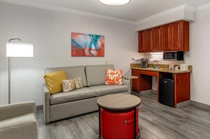 Uma sala de estar moderna com um sofá cinza, um tambor vermelho e uma área de cozinha com armários de madeira e um micro-ondas.