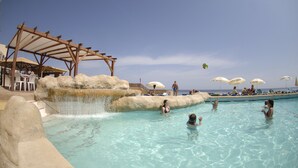 Uma área de piscina com água cristalina, uma pérgula de madeira e guarda-sóis.
