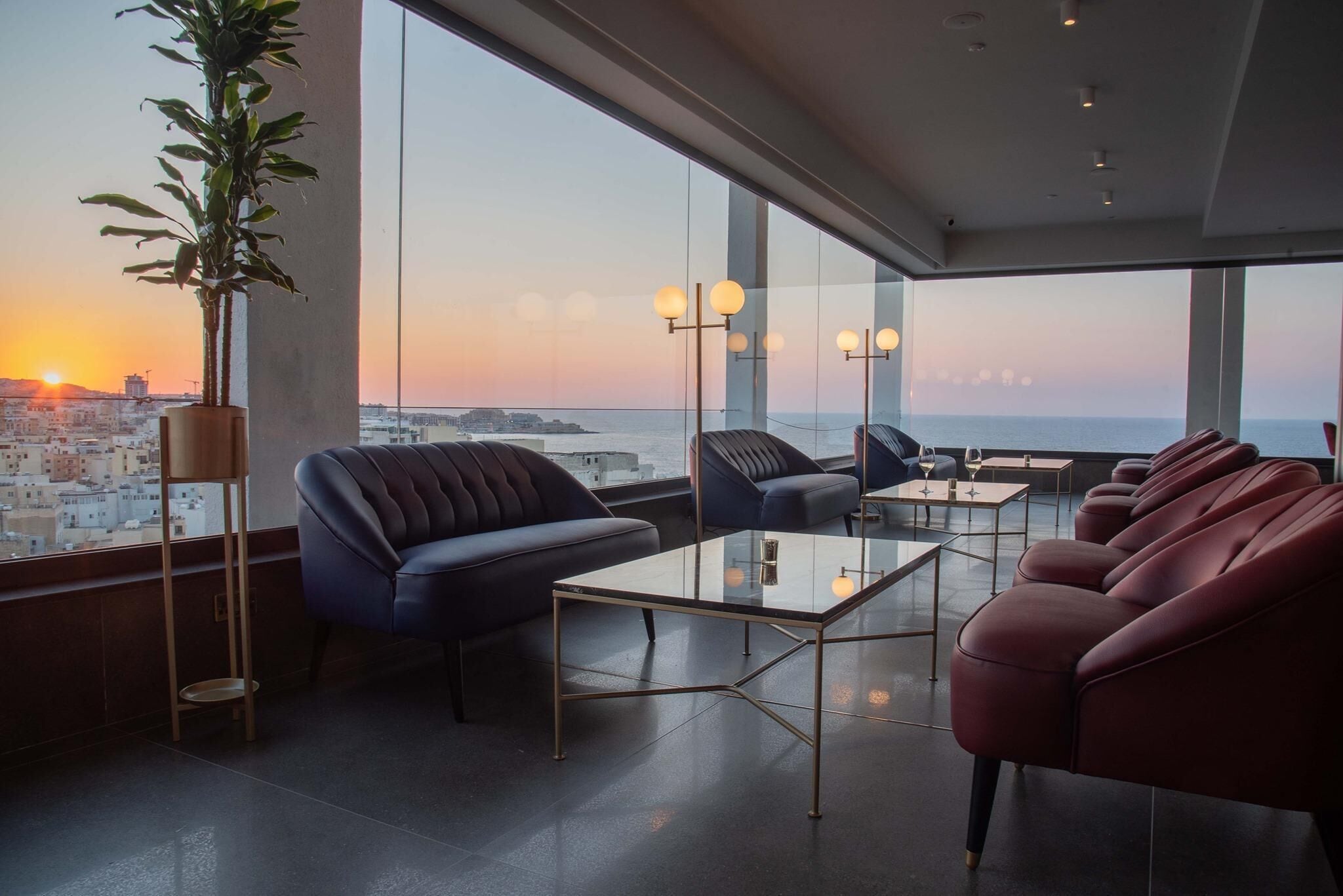 Uma sala de estar moderna com sofás de couro, uma mesa de centro de vidro e vista para o pôr do sol sobre a cidade.