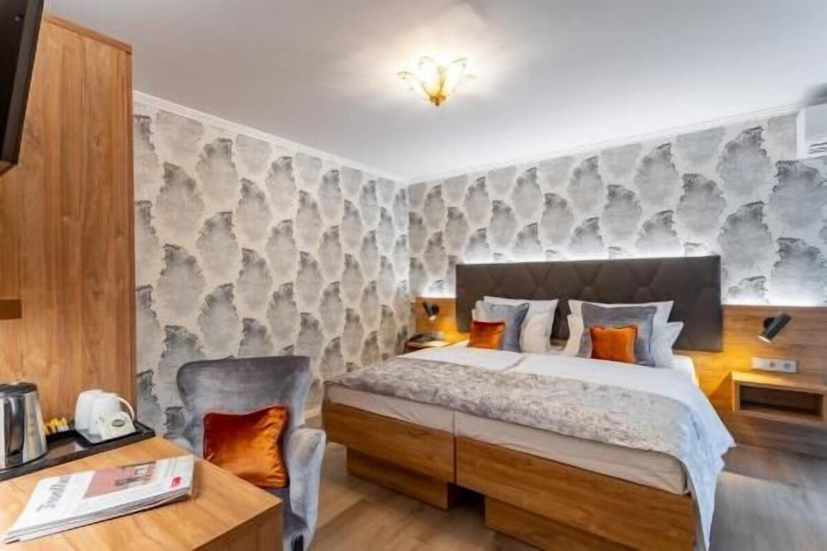 Quarto com parede estampada em pedra, cama com vários travesseiros, mesa de cabeceira de madeira e uma cadeira.