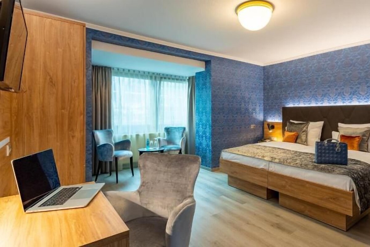 Quarto de hotel com uma cama, uma mesa com um laptop, uma cadeira e vista para o exterior.