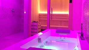 Um spa moderno com uma banheira grande e uma área de chuveiro separada, ambos iluminados por iluminação roxa.
