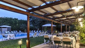 Um pátio externo com piscina, espreguiçadeiras e mesas dispostas para refeições.