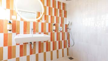 Casa de banho com lavatório branco, espelho redondo, chuveiro e parede revestida a mosaicos xadrez.