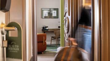Um corredor de hotel com uma porta, uma cadeira, uma mesa e quadros nas paredes.